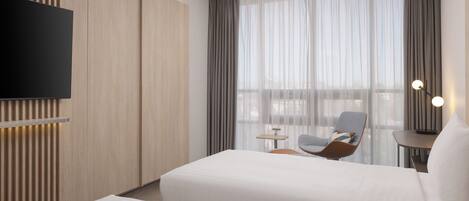 Quarto de hotel com duas camas, televisão de tela plana, uma mesinha, uma cadeira e janela com cortinas.