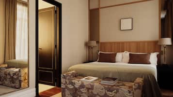 Quarto de hotel com cama, abajures, mesa de cabeceira com um livro, sofá e espelho.
