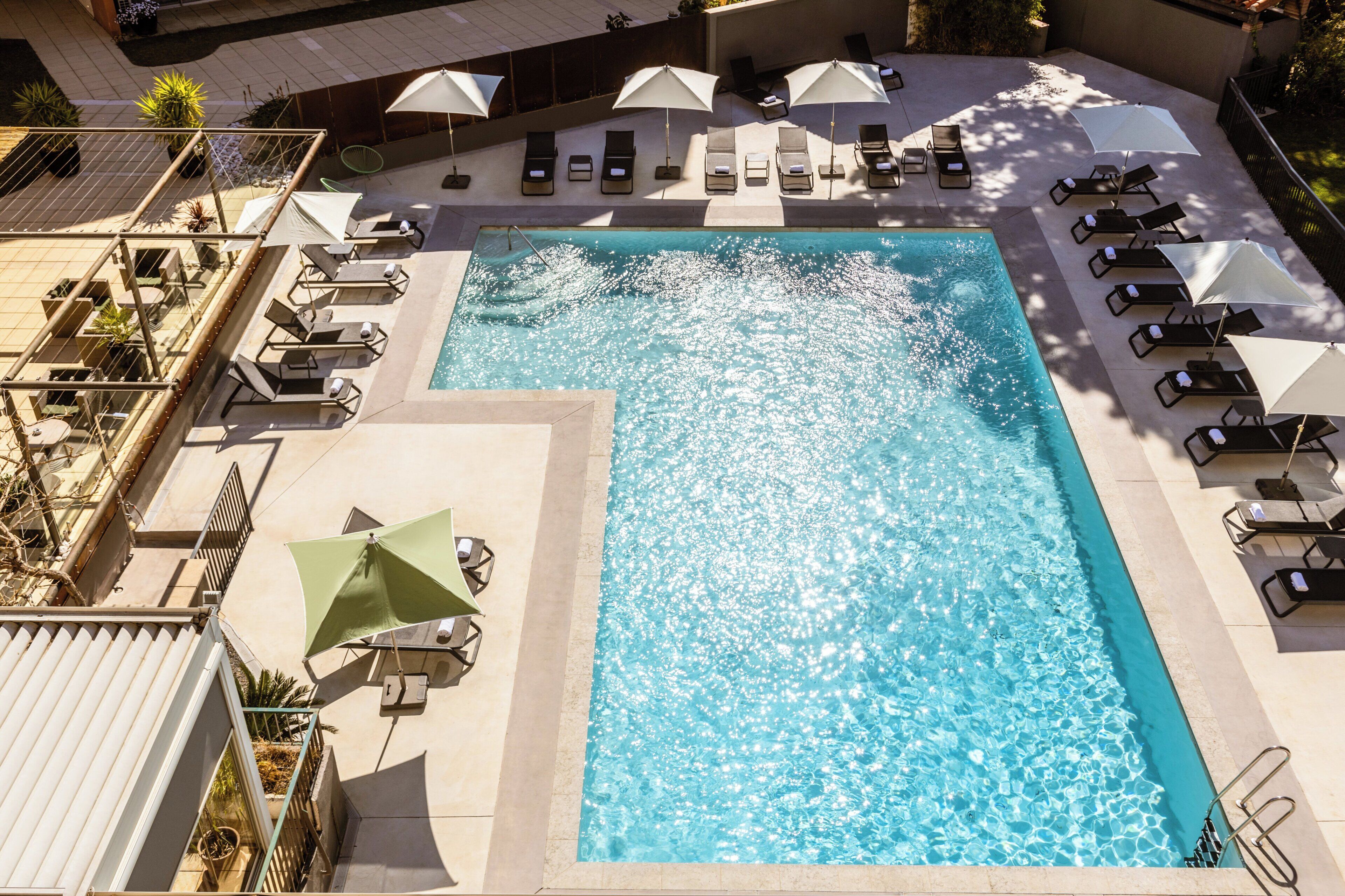Piscina com vários espreguiçadeiras e guarda-sóis, ladeada por um deck revestido com azulejos.