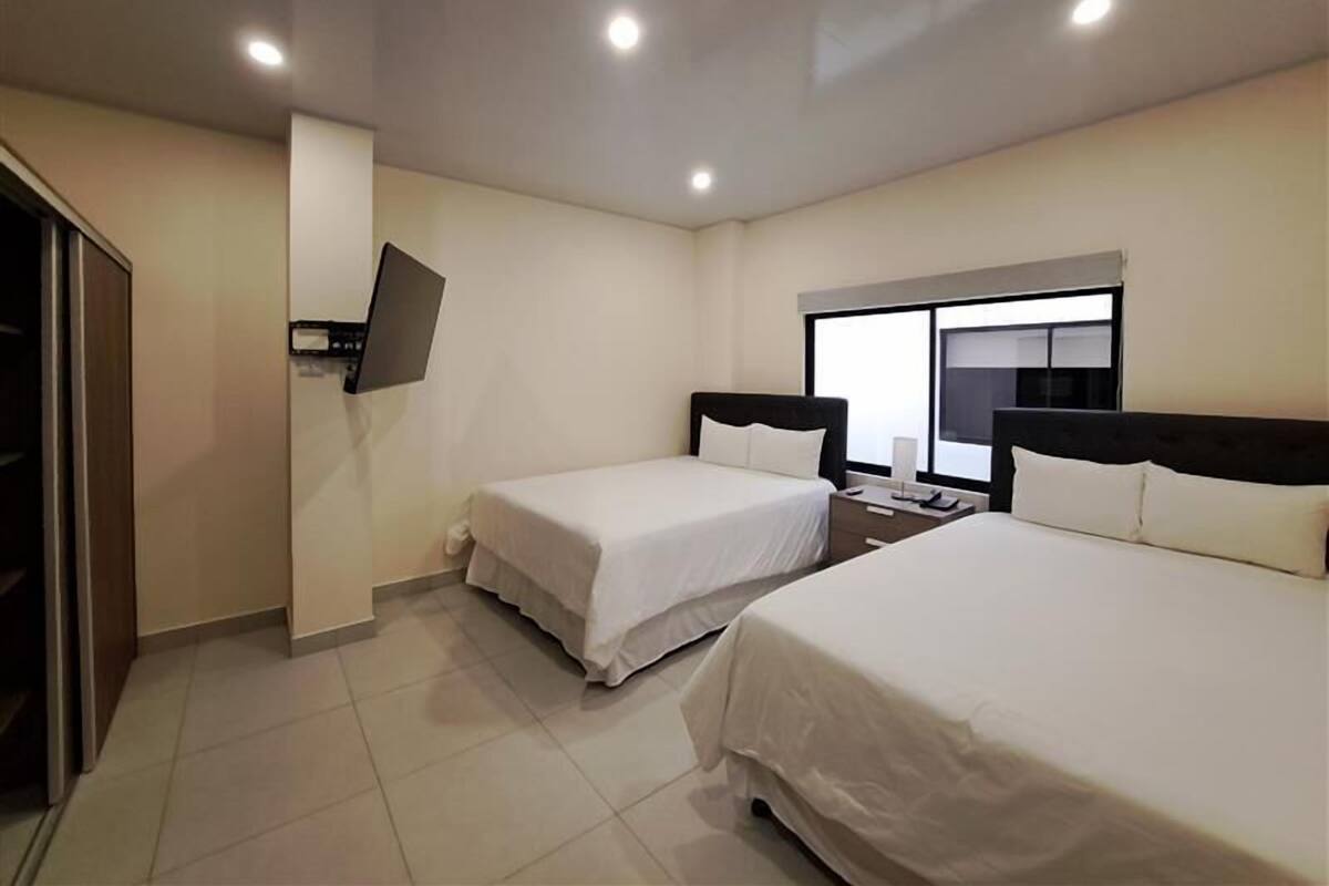 Quarto de hotel com duas camas, televisão fixada na parede e janela com persianas.