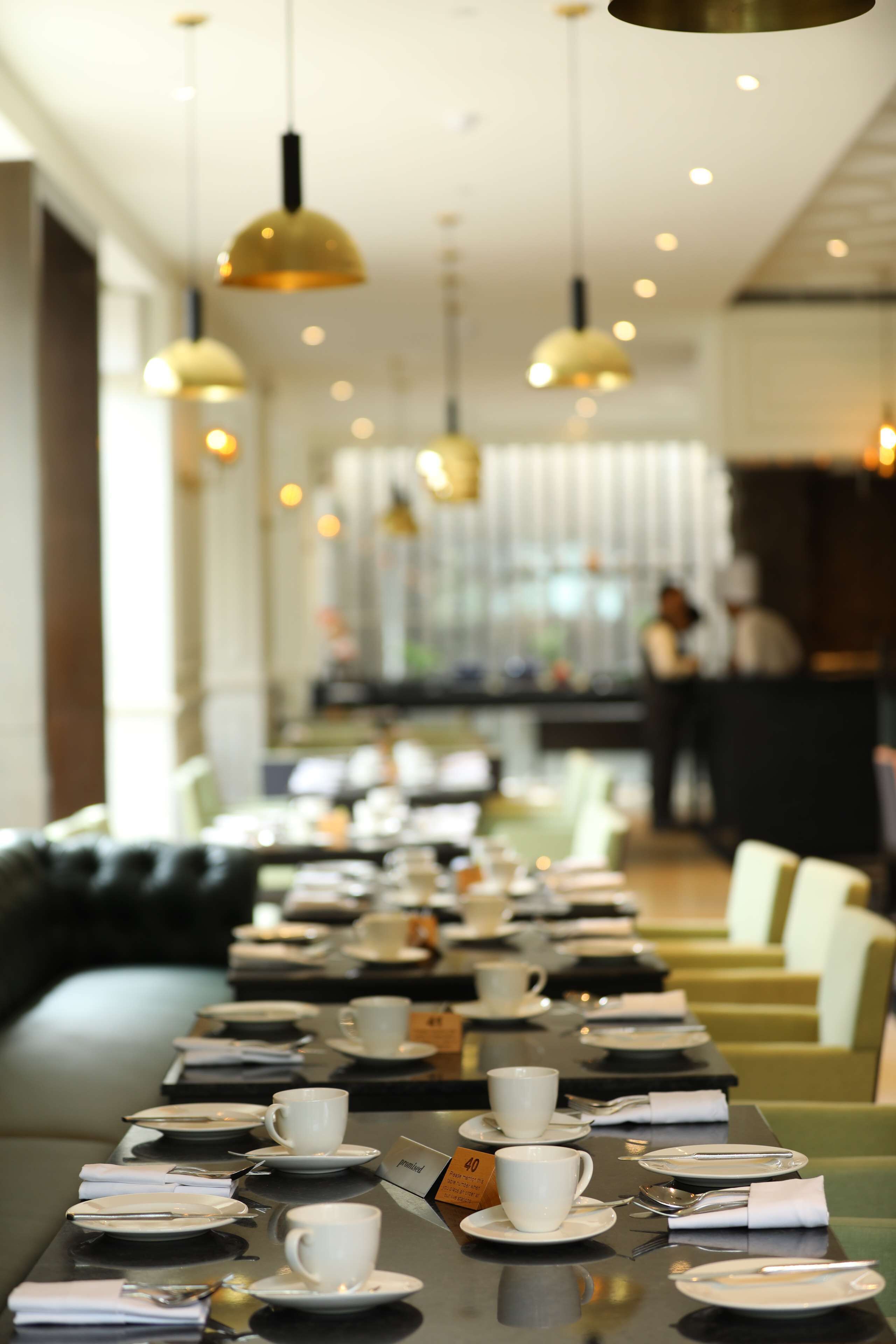 Um restaurante com mesas preparadas para refeições, apresentando um balcão comprido e assentos acolchoados.