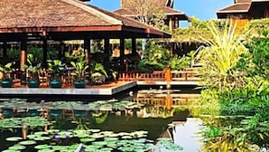 Um resort com área de estar coberta ao ar livre, um lago com nenúfares e vegetação exuberante.