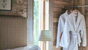 Quarto estilo cabana de madeira com cama, almofadas, luminária e roupão pendurado em um suporte.