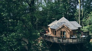 Uma casa na árvore de madeira com telhado inclinado, rodeada por uma floresta densa.