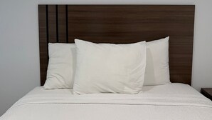 Cama com cabeceira de madeira, roupa de cama branca e duas almofadas.