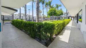 Um edifício moderno com design geométrico, um caminho pavimentado e um jardim bem cuidado com palmeiras.