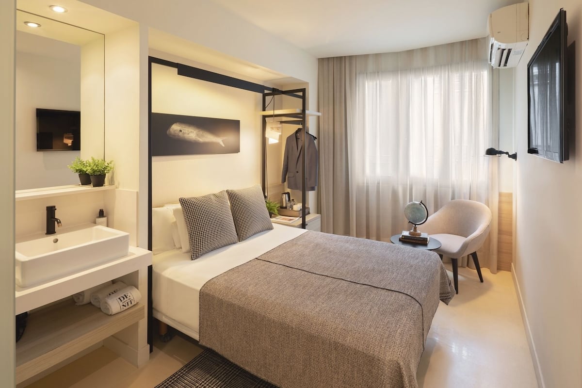 Quarto de hotel moderno com uma cama grande, mesa de cabeceira, espelho, cômoda e janela com cortinas.