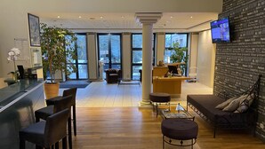Um hall amplo com balcão de recepção, área de estar e grandes janelas com vista para a cidade.