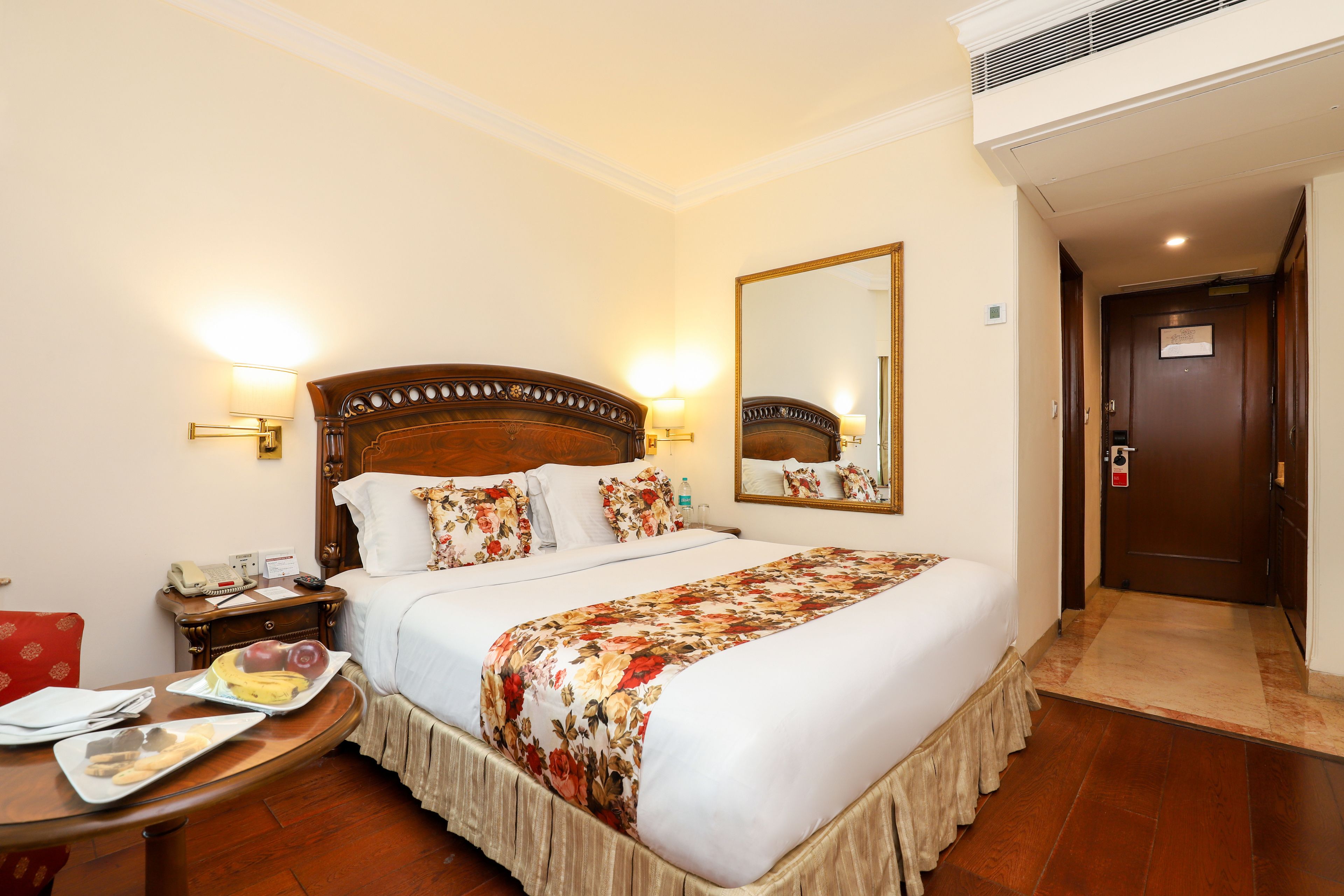 Quarto de hotel com uma cama grande, mesas de cabeceira, um espelho e uma porta que dá para o corredor.