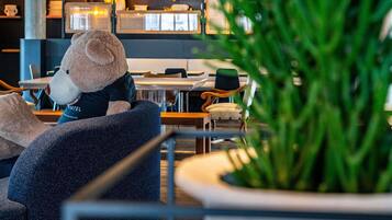 Um urso de pelúcia em um saguão de hotel, com assentos e uma grande planta em vaso.