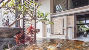 Piscina interior moderna com água cristalina, rodeada por plantas em vasos e uma bacia de pedra.