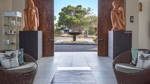 Uma área de recepção com duas grandes portas de madeira, um balcão de atendimento e duas cadeiras de vime com almofadas.