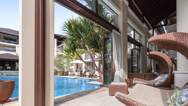 Área de piscina com móveis de vime e vista para a piscina e palmeiras.