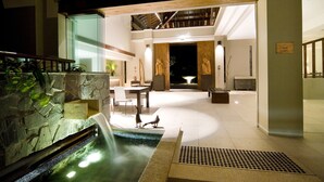Um interior moderno com um elemento aquático de pedra, uma área de refeições e uma mesa de recepção.