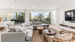 Uma sala de estar moderna com um sofá seccional, uma TV, cadeiras de vime e um espaço de refeições com mesa e cadeiras.