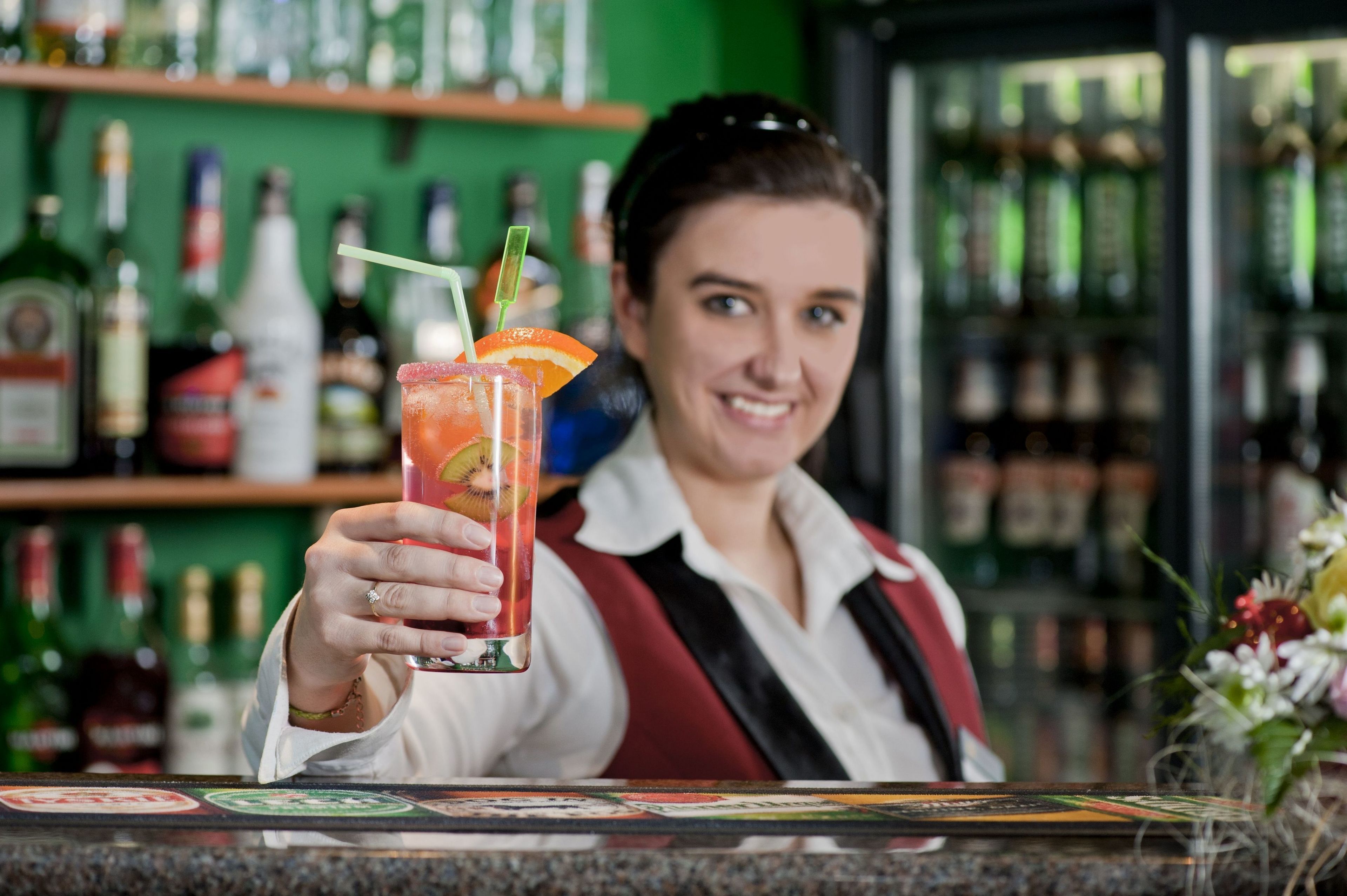 Um bartender segurando um coquetel com canudo e uma fatia de laranja.
