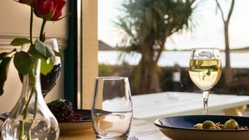 Uma mesa de jantar com um vaso de rosas, uma tigela de frutas e um copo de vinho branco.