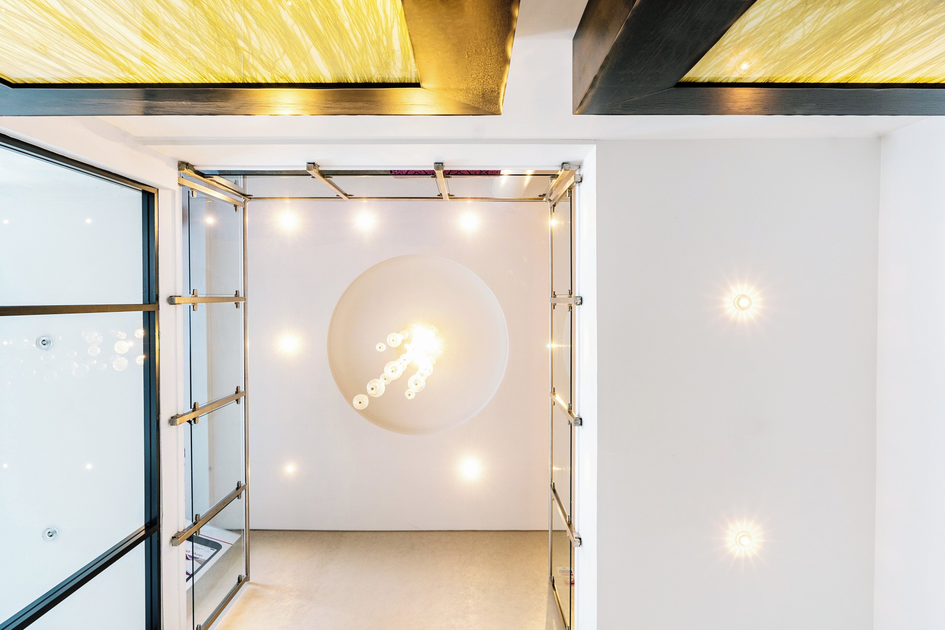 Quarto moderno com porta de vidro, luminária circular na parede e teto com vigas aparentes.