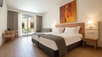 Quarto de hotel com uma cama grande, cabeceira de madeira, mesa de cabeceira com abajur, um banco e uma porta de vidro deslizante para uma área externa.