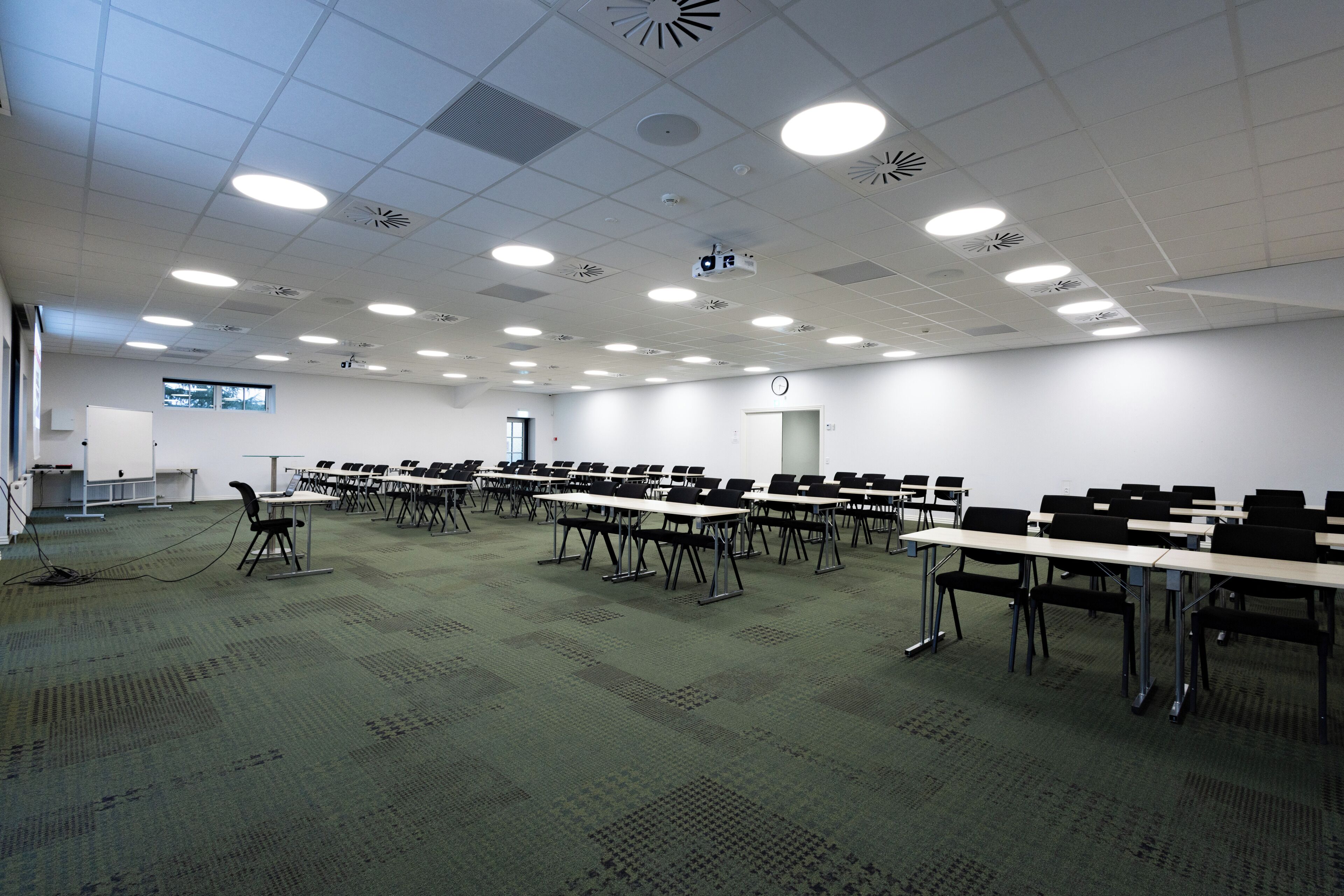 Uma sala de conferência com várias mesas e cadeiras, luminárias no teto e uma tela de projeção.