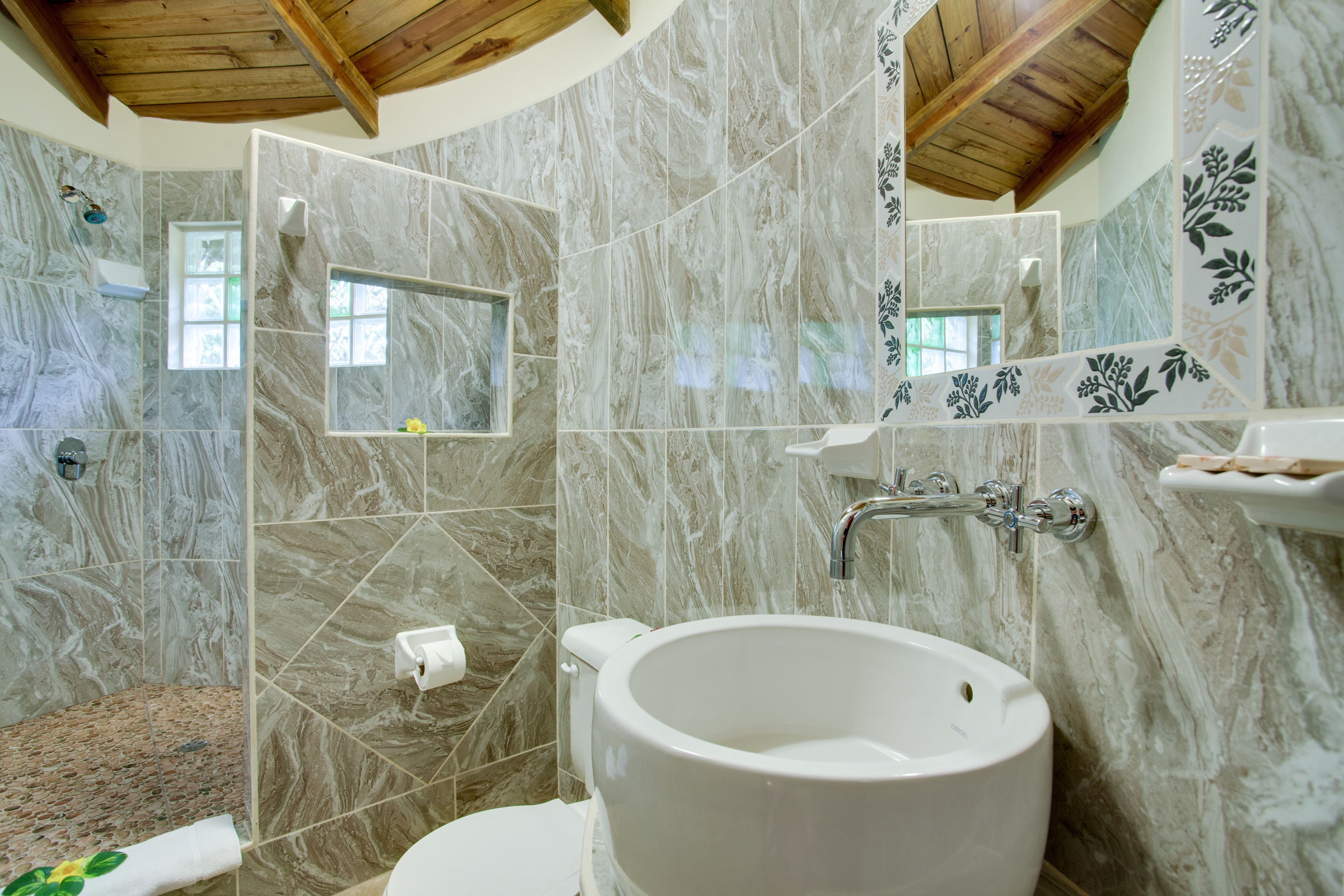 Um banheiro com uma grande pia de mármore, um chuveiro com porta de vidro e um espelho com detalhes de azulejos florais.