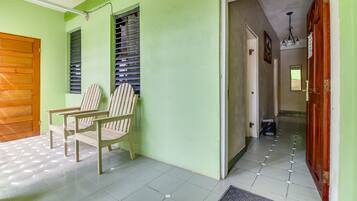 Um quarto com parede verde, porta de madeira, janela com persianas, uma cadeira e chão de azulejos.