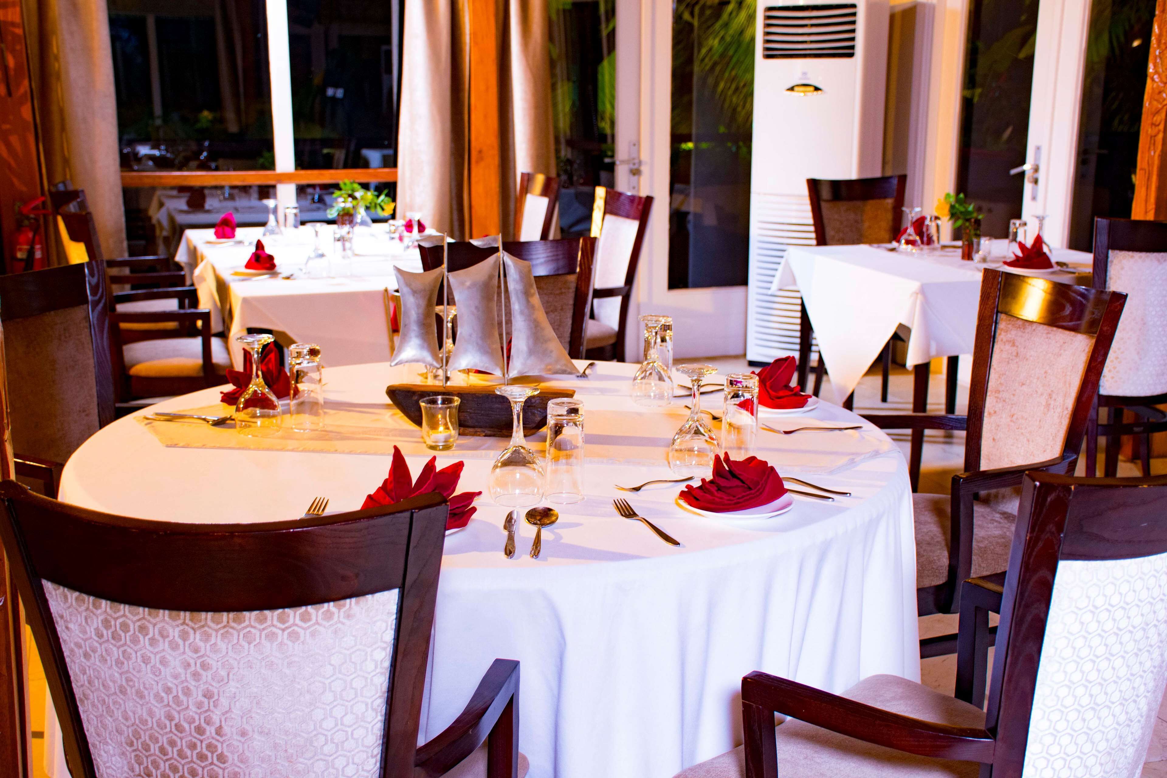 Restaurante com mesas redondas preparadas para refeições, com toalhas de mesa brancas e cadeiras de madeira.