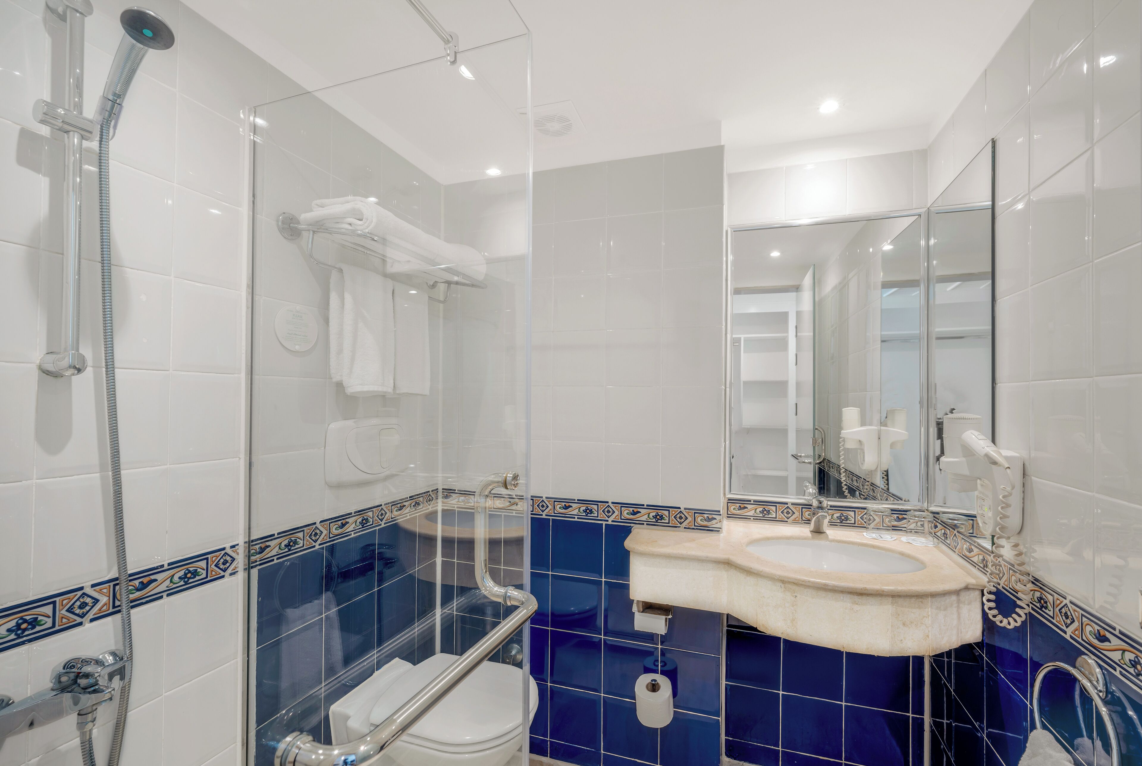 Casa de banho com chuveiro em cabine de vidro, sanita branca e lavatório com painel de azulejos azuis.