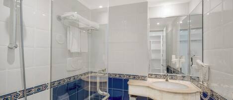 Casa de banho com chuveiro em cabine de vidro, sanita branca e lavatório com painel de azulejos azuis.