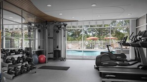 Uma academia com esteiras, halteres e bolas de exercício, com vista para uma piscina.