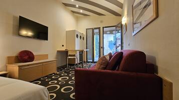 Quarto de hotel com cama, escrivaninha, cadeira, televisão, sofá e vista para o exterior.