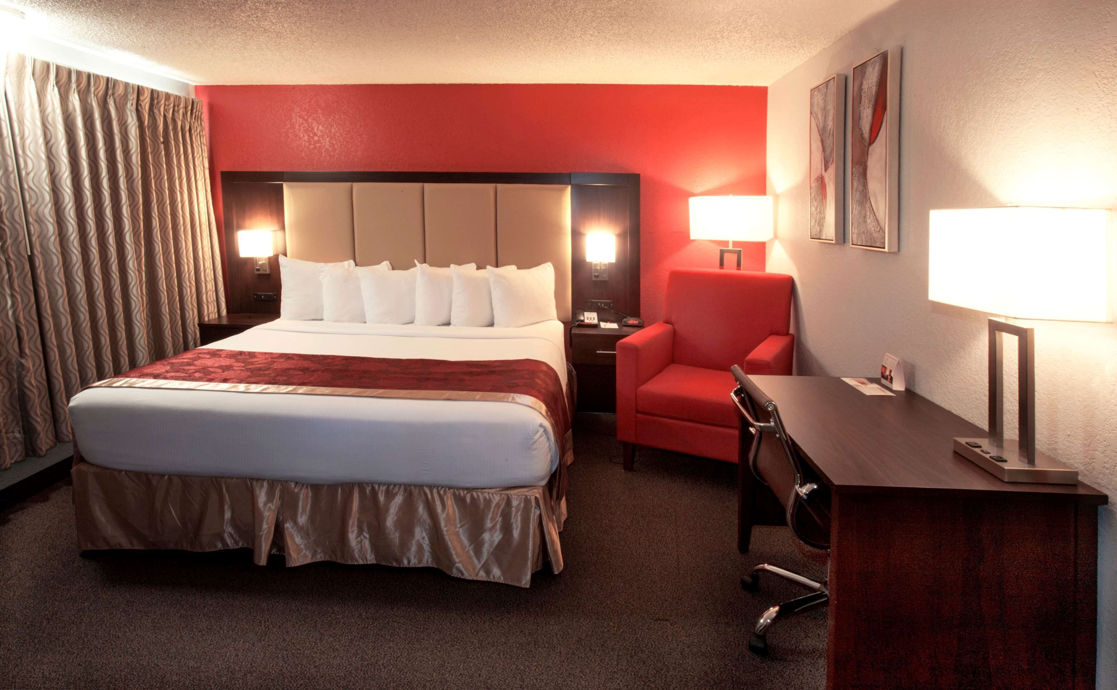Quarto de hotel com uma cama grande, uma escrivaninha, uma cadeira e uma mesa de cabeceira com abajur.