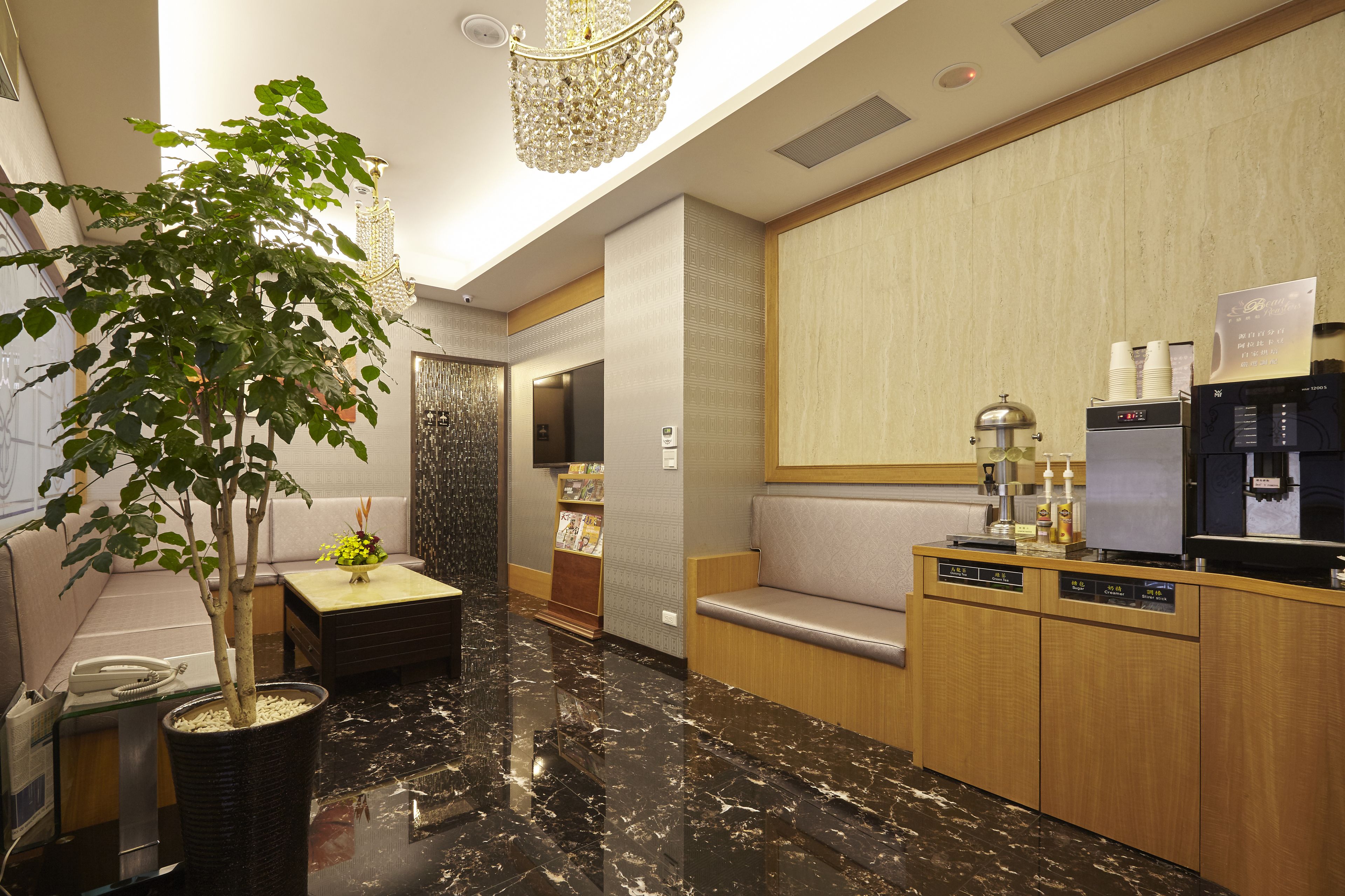 Um hall de hotel moderno com piso de mármore, um balcão de recepção, área de estar, uma planta em vaso e um candelabro.