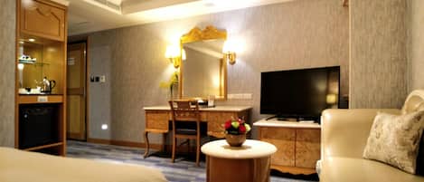 Quarto de hotel com cama, sofá, escrivaninha com cadeira, televisão e espelho.