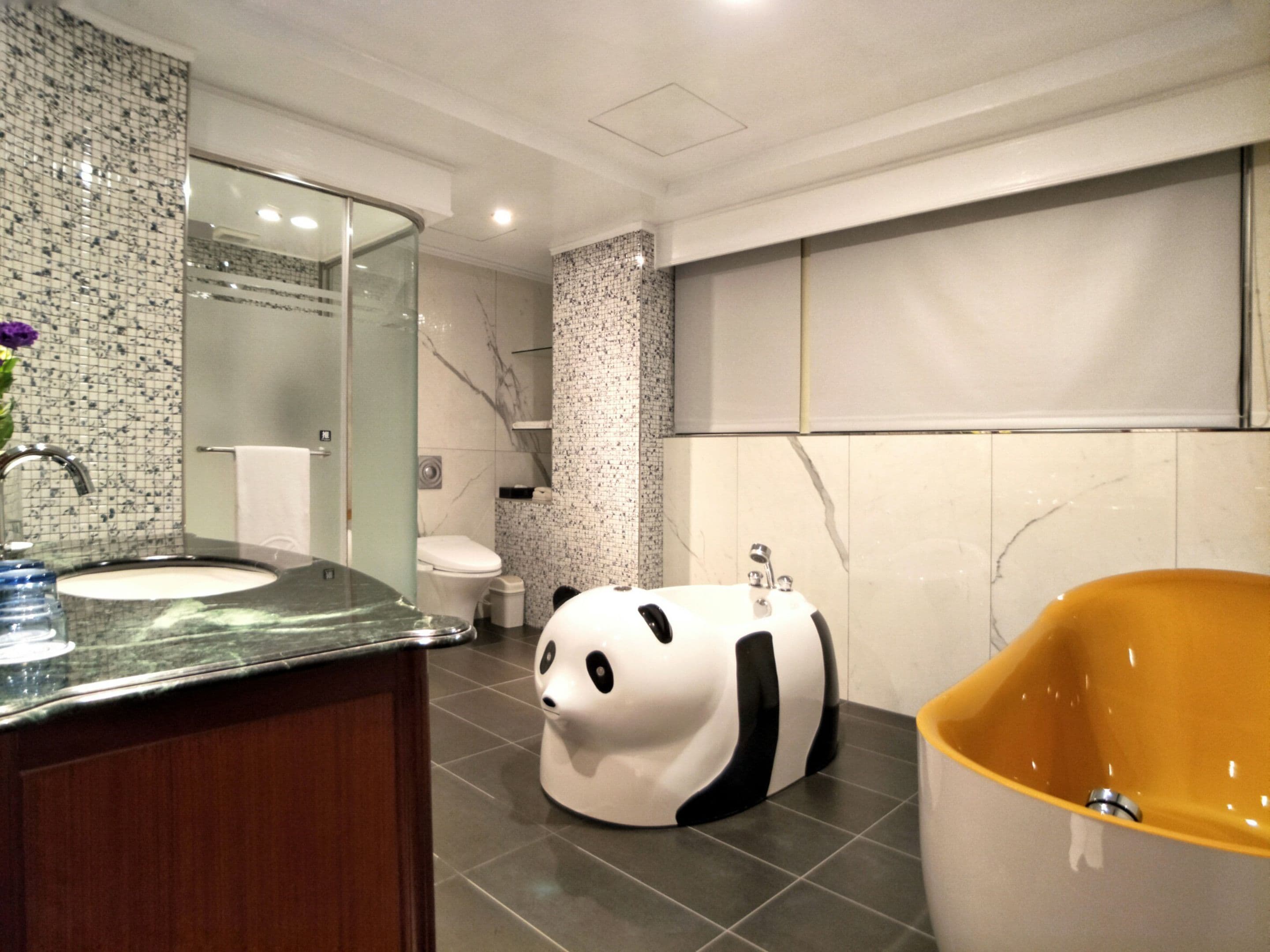 Um banheiro com pia de mármore, vaso sanitário, banheira em formato de panda e espelho.