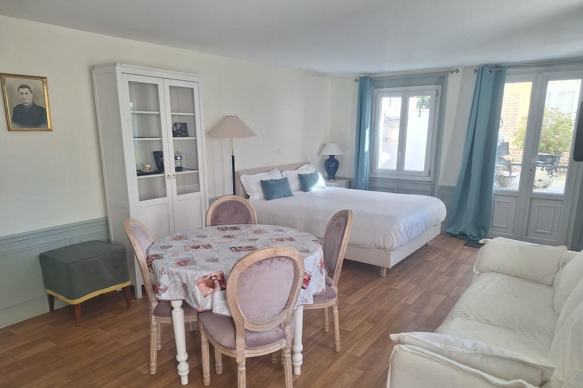 Quarto com cama, mesa de cabeceira, abajur, guarda-roupa, mesa de jantar com cadeiras e janela com cortinas.
