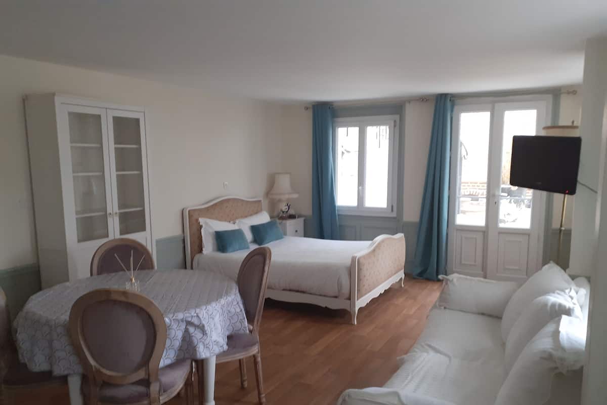 Quarto de hotel com duas camas, uma mesa de jantar, cadeiras, televisão e janela com cortinas.