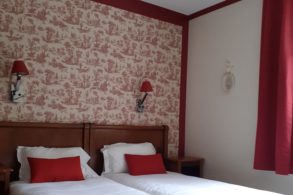 Uma cama de casal com roupa de cama branca e almofadas vermelhas, uma cabeceira de madeira e um papel de parede estampado.