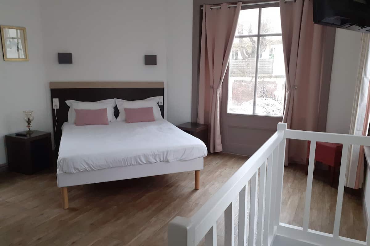 Quarto com cama, mesas de cabeceira, janela com cortinas e vista para o exterior.