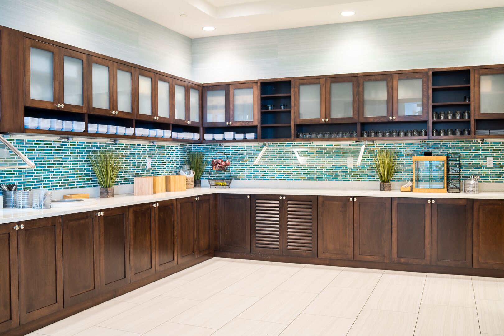Cozinha moderna com armários de madeira escura, painel de azulejos e bancada branca.
