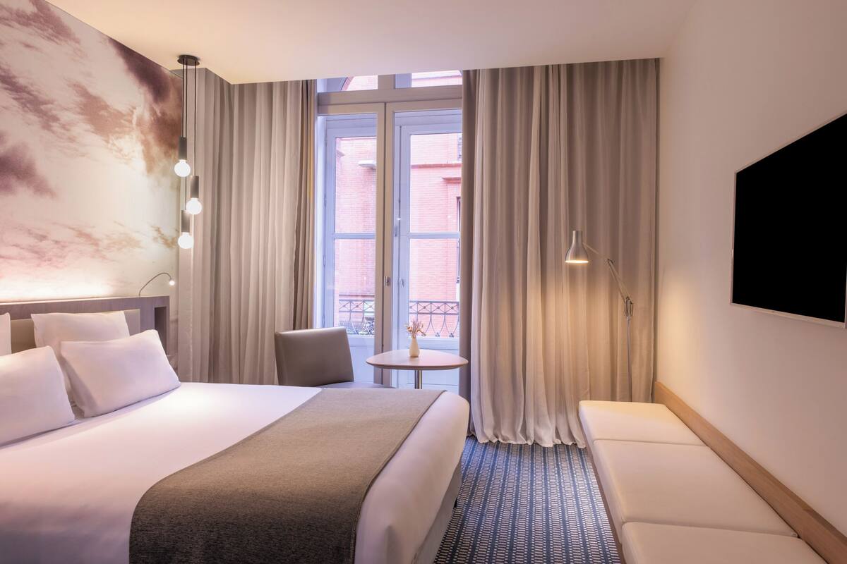 Quarto de hotel com uma cama grande, uma mesa pequena com um vaso, uma cadeira e um sofá.