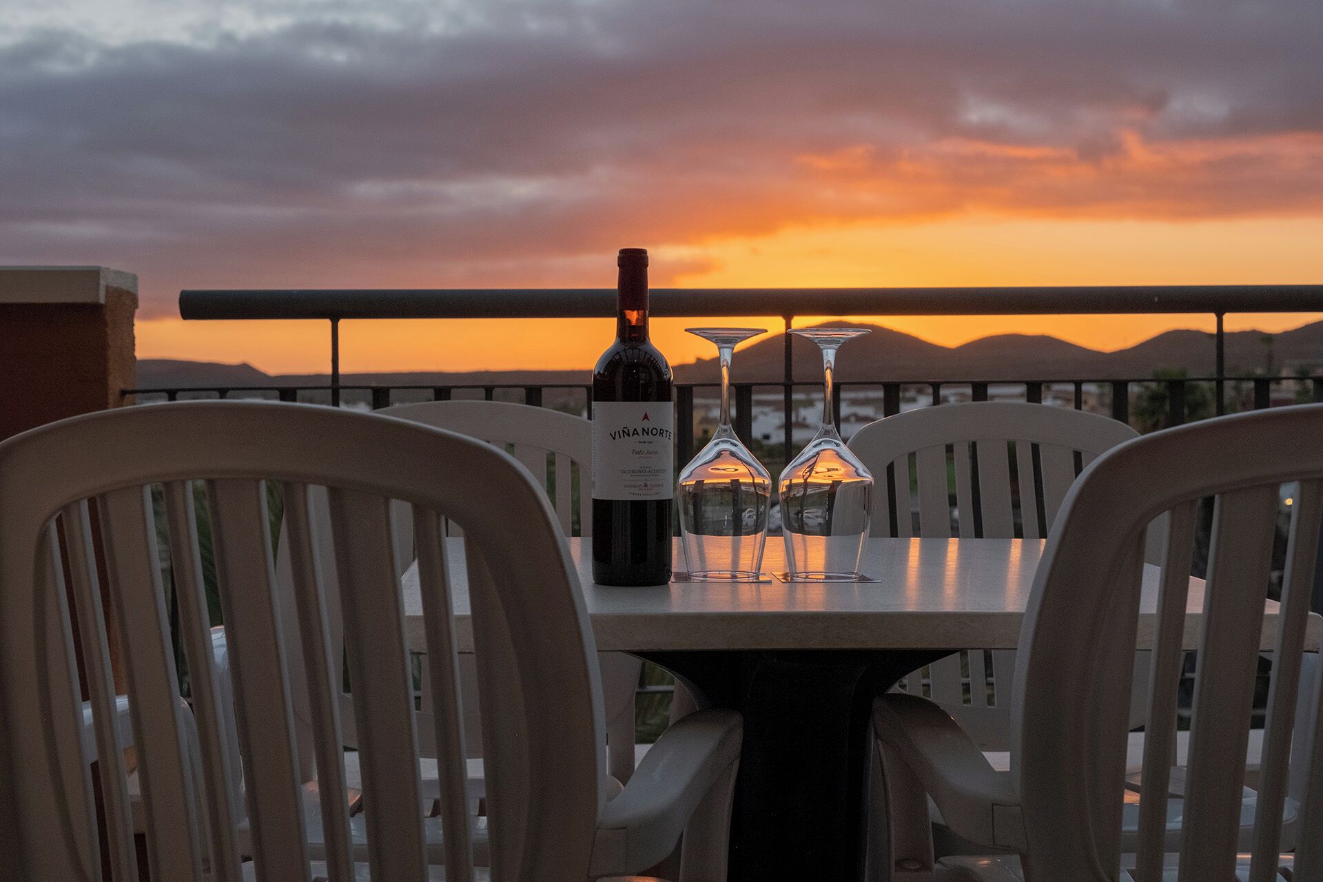 Mesa com garrafa e dois copos, com vista para o pôr do sol.