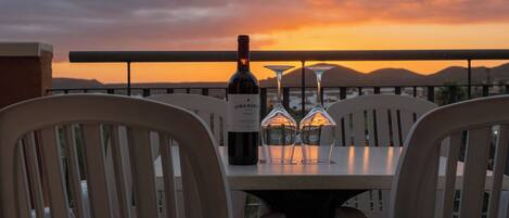 Mesa com garrafa e dois copos, com vista para o pôr do sol.