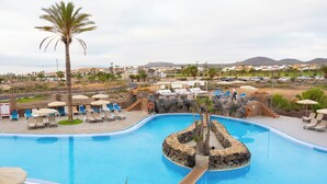 Piscina com espreguiçadeiras e guarda-sóis, cercada por paisagem rochosa e palmeiras.