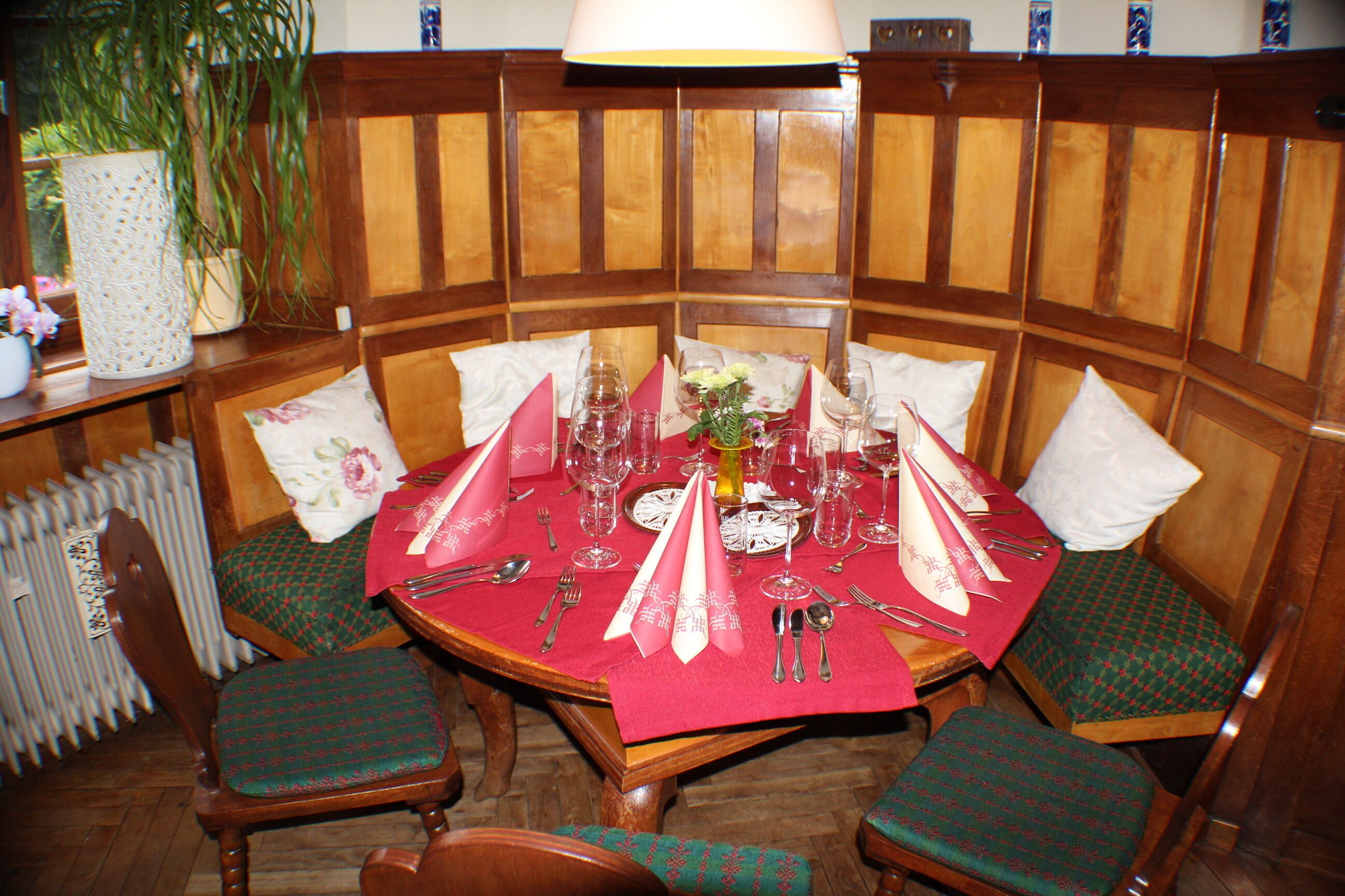 Uma sala de jantar com uma mesa redonda posta para quatro pessoas, rodeada por cadeiras de madeira com almofadas verdes.
