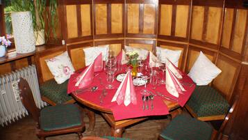 Uma sala de jantar com uma mesa redonda posta para quatro pessoas, rodeada por cadeiras de madeira com almofadas verdes.