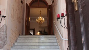 Uma escadaria de mármore com um candelabro no topo, dando acesso a uma porta.