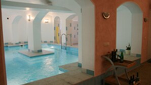 Piscina interna com água cristalina, rodeada por paredes e arcos brancos.