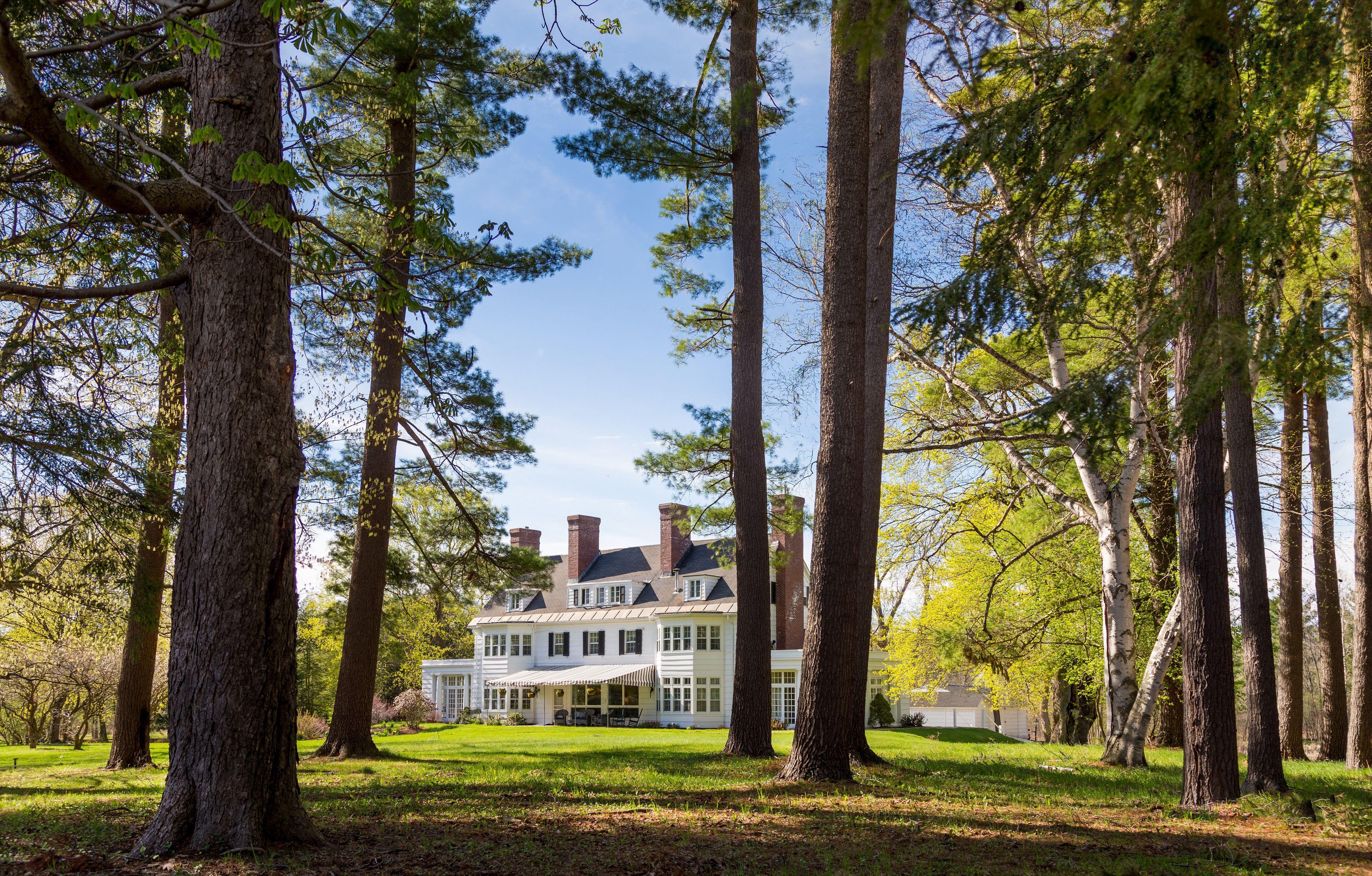 Uma casa grande e histórica, cercada por árvores altas em um jardim bem cuidado.