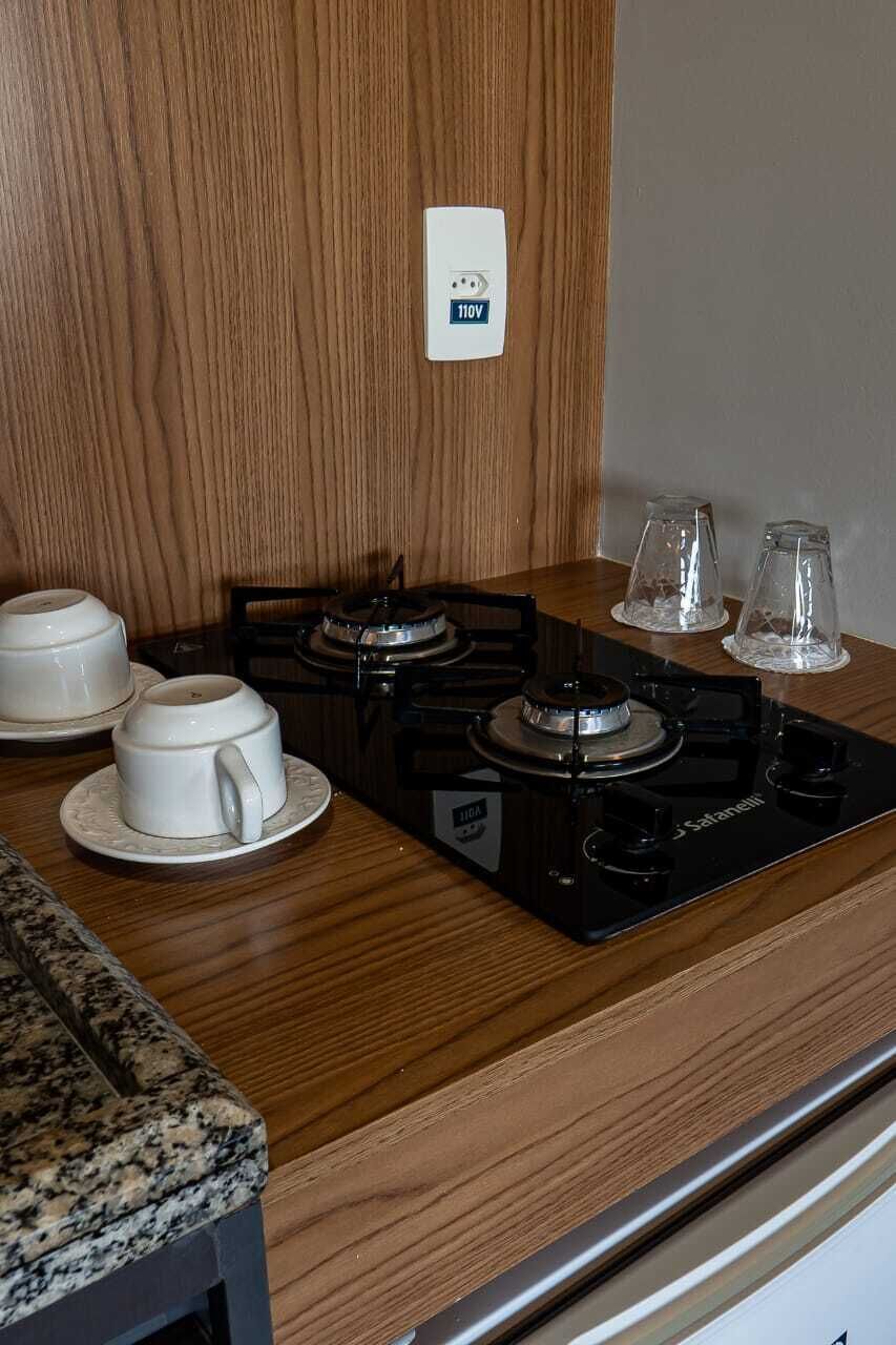 Uma cozinha com fogão a gás, uma tomada e três xícaras brancas em uma bancada de madeira.